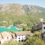 Guadalest Castle perched dramatically on rocky cliffs above a turquoise lake with mountains in the background
