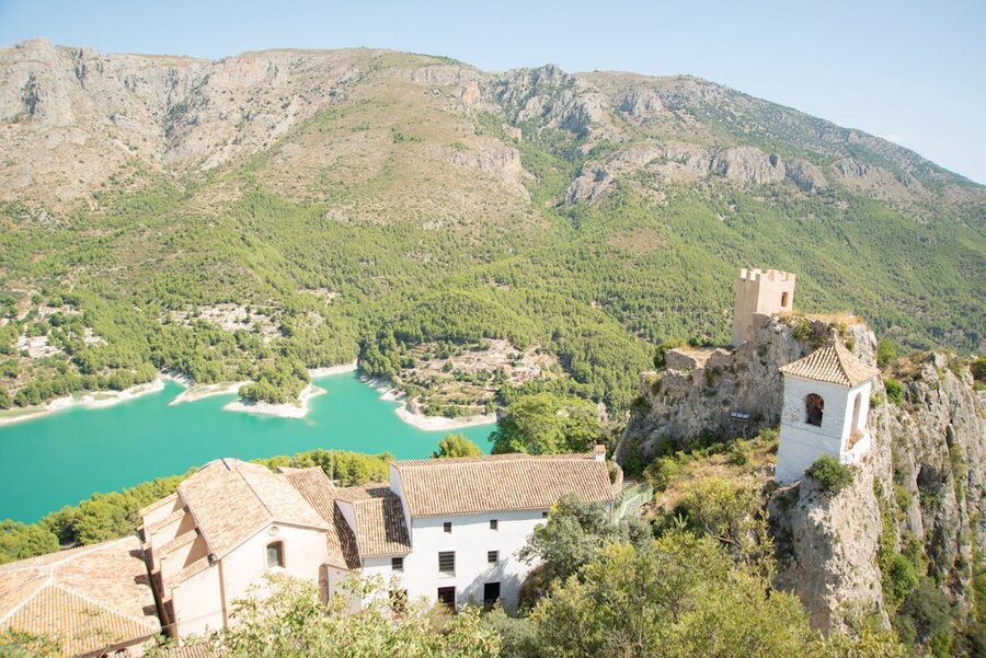 Guadalest Castle perched dramatically on rocky cliffs above a turquoise lake with mountains in the background