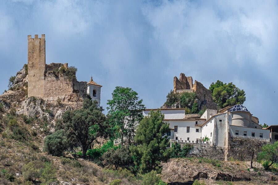 View of Guadalest Castle and village surrounded by dense green vegetation under clear blue sky