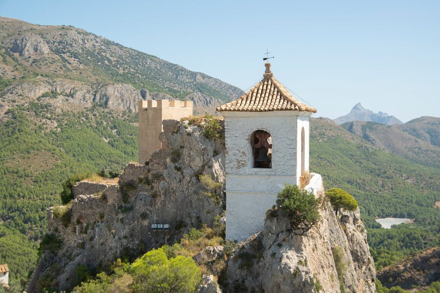 Historic Guadalest Castle perched on dramatic rocky cliffs against a clear blue summer sky in Spain
