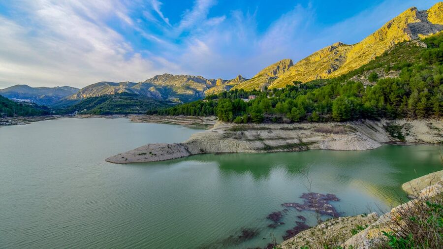 Wide landscape view of Guadalest lake with mountains in the background under summer skies in Spain