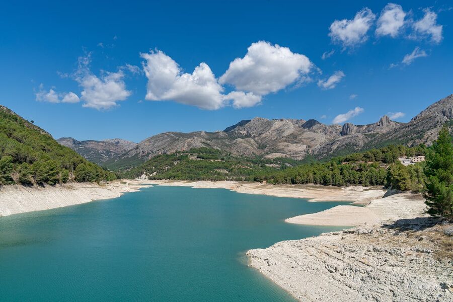 The turquoise Embalse de Guadalest reservoir surrounded by green mountains and clear blue skies
