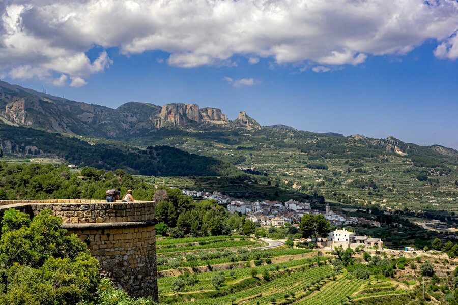 Verdant Guadalest Valley with lush green agricultural fields, scattered buildings, and mountains in the distance