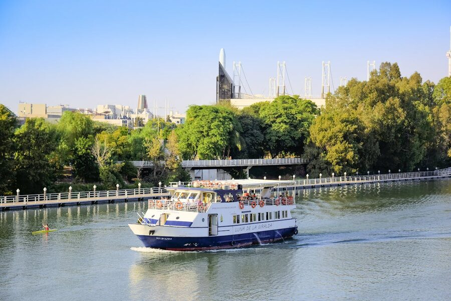 A sightseeing cruise boat on the Guadalquivir River passing historic Seville buildings
