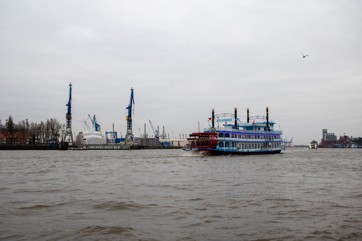 A paddle steamer sailing on the Elbe River in Hamburg with port activity in the background