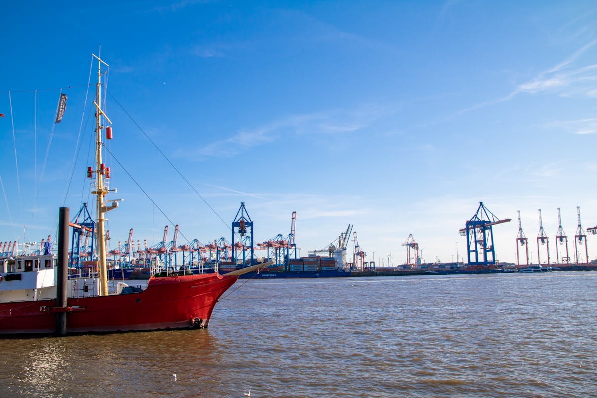 Red sailboat with industrial cranes at Hamburg harbor on a sunny day