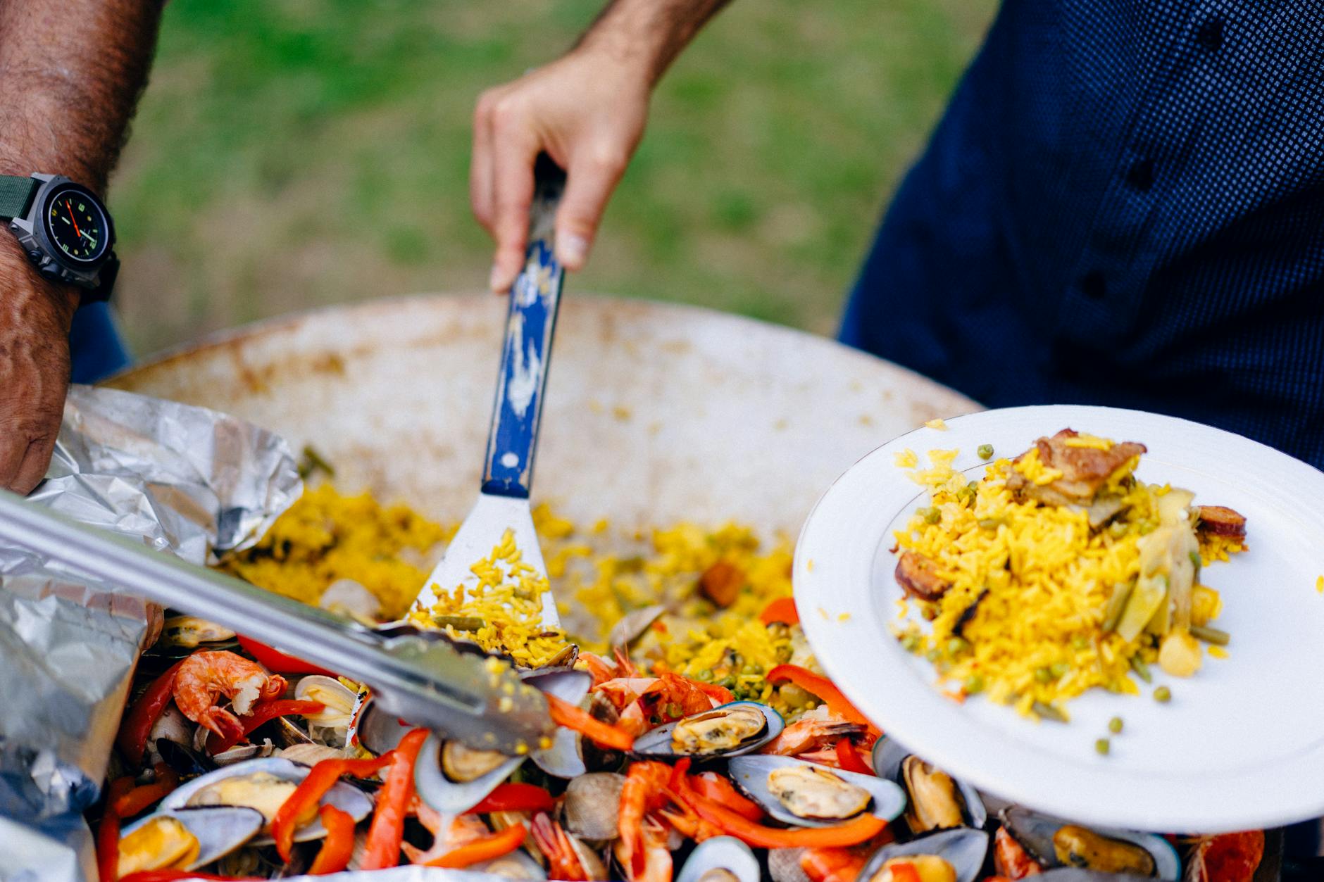 Close-up of hands serving Spanish paella with shrimp and mussels from a pan