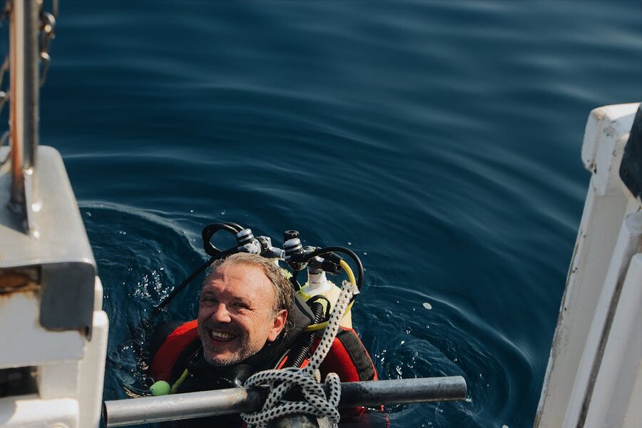 A joyful scuba diver emerges from the ocean smiling at the camera