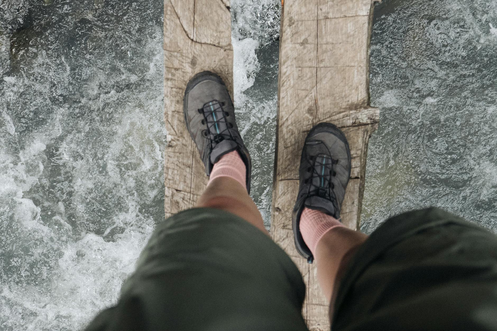Hiker crossing a rustic wooden bridge over rushing mountain river