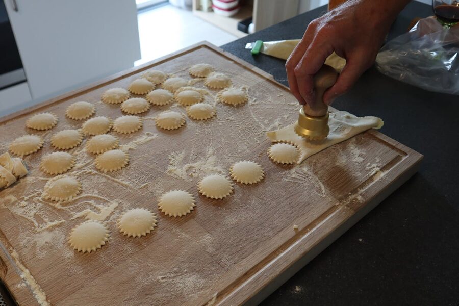 Person making homemade ravioli with a pasta cutter on a floured wooden board