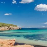 Clear turquoise water lapping against a sandy Ibiza beach under bright blue skies