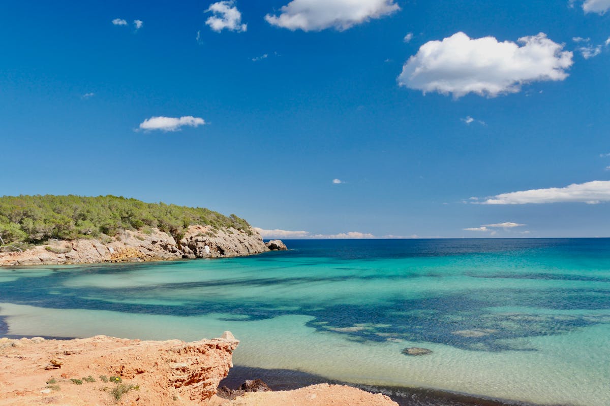 Clear turquoise water lapping against a sandy Ibiza beach under bright blue skies