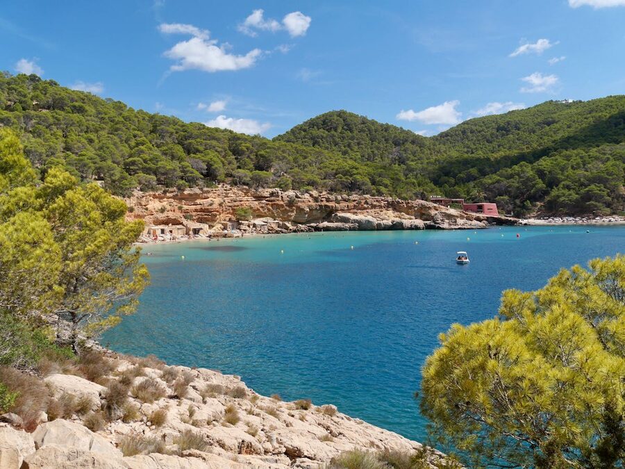 Serene turquoise bay in Ibiza surrounded by green hills with boats anchored