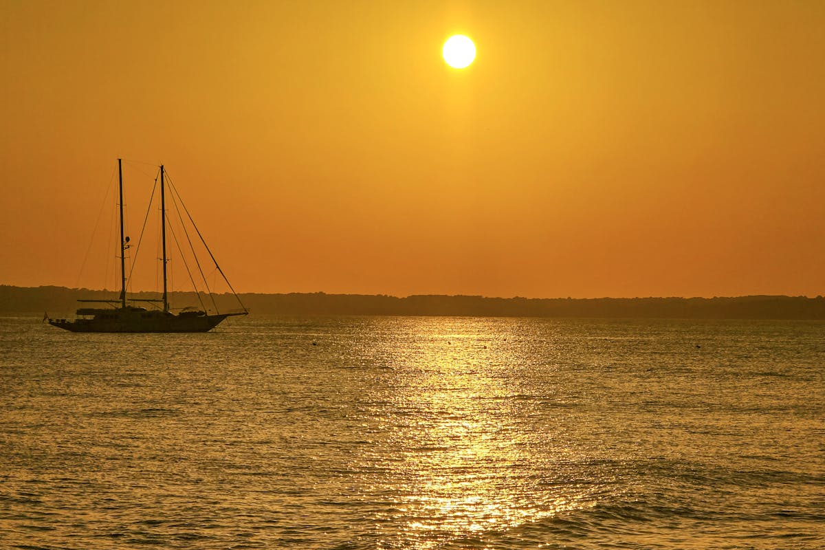 A sailboat on calm water during a golden sunset in Ibiza, Spain