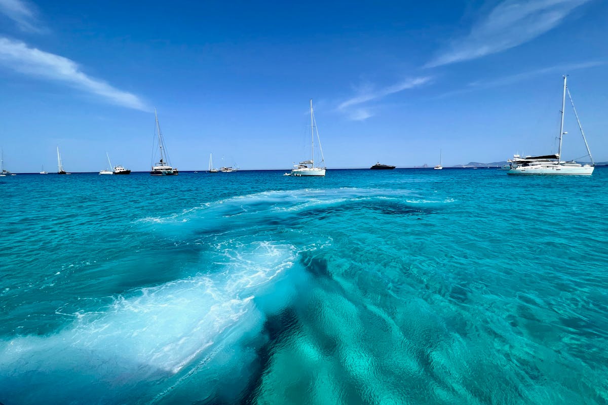 Several sailboats floating on crystal clear turquoise waters near Ibiza
