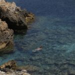 Woman snorkeling near rocky cliffs in crystal clear Ibiza waters