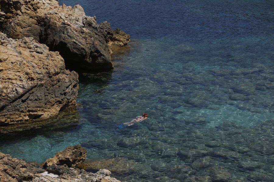 Woman snorkeling near rocky cliffs in crystal clear Ibiza waters