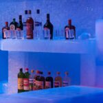 Liquor bottles and glasses displayed on ice shelves under blue lighting inside an ice bar