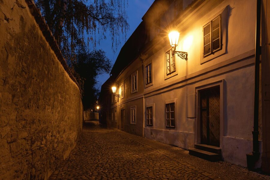 Narrow cobblestone street in Prague Old Town lit by warm lantern light at night