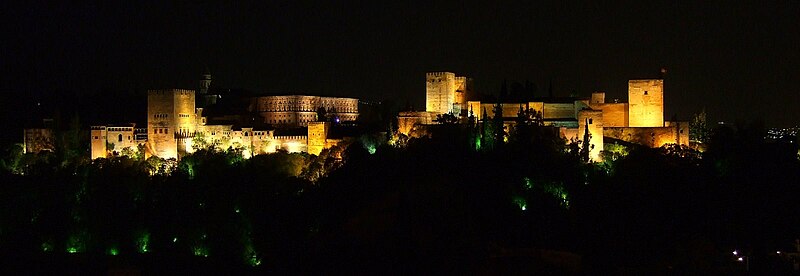 The Alhambra palace lit up at night against a dark sky in Granada Spain