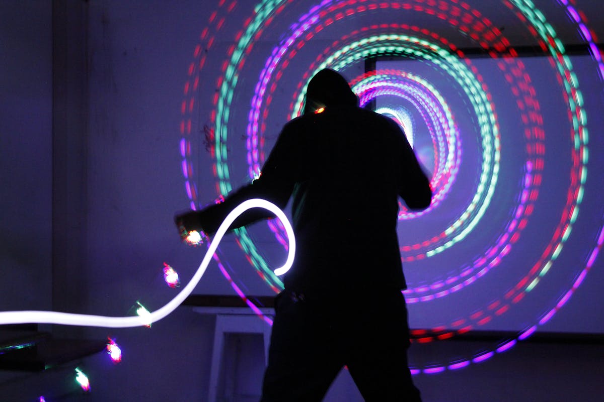 Silhouette of a performer spinning colorful LED poi in a dark room