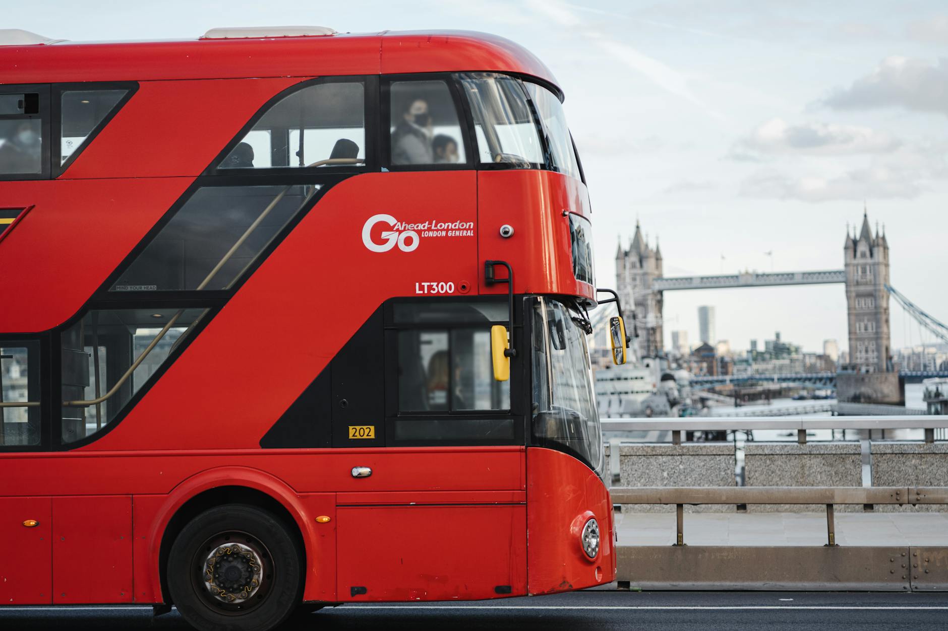 Red double decker bus driving along a calm river with historic London buildings