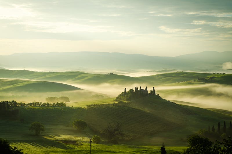 Early morning mist floating through Tuscan hills and valleys with a farmhouse in the distance