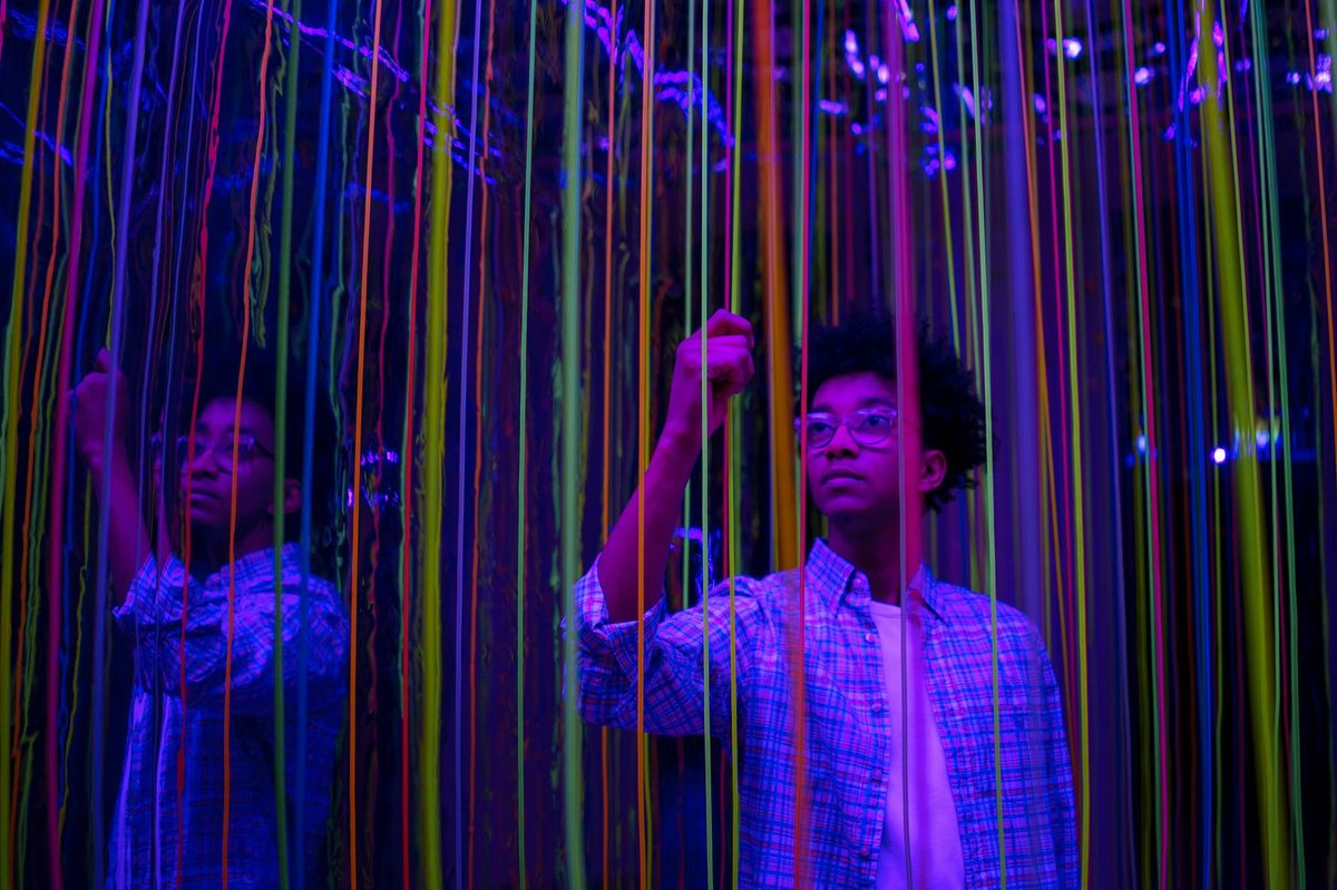 A young person with colorful neon strings in a reflective installation