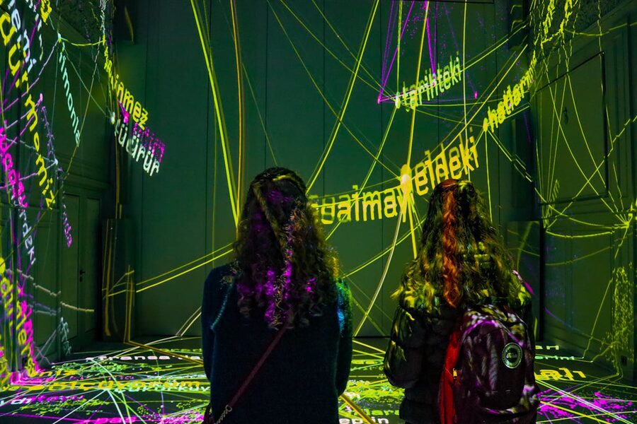 Two women observing dynamic text projection art installation in a dark room