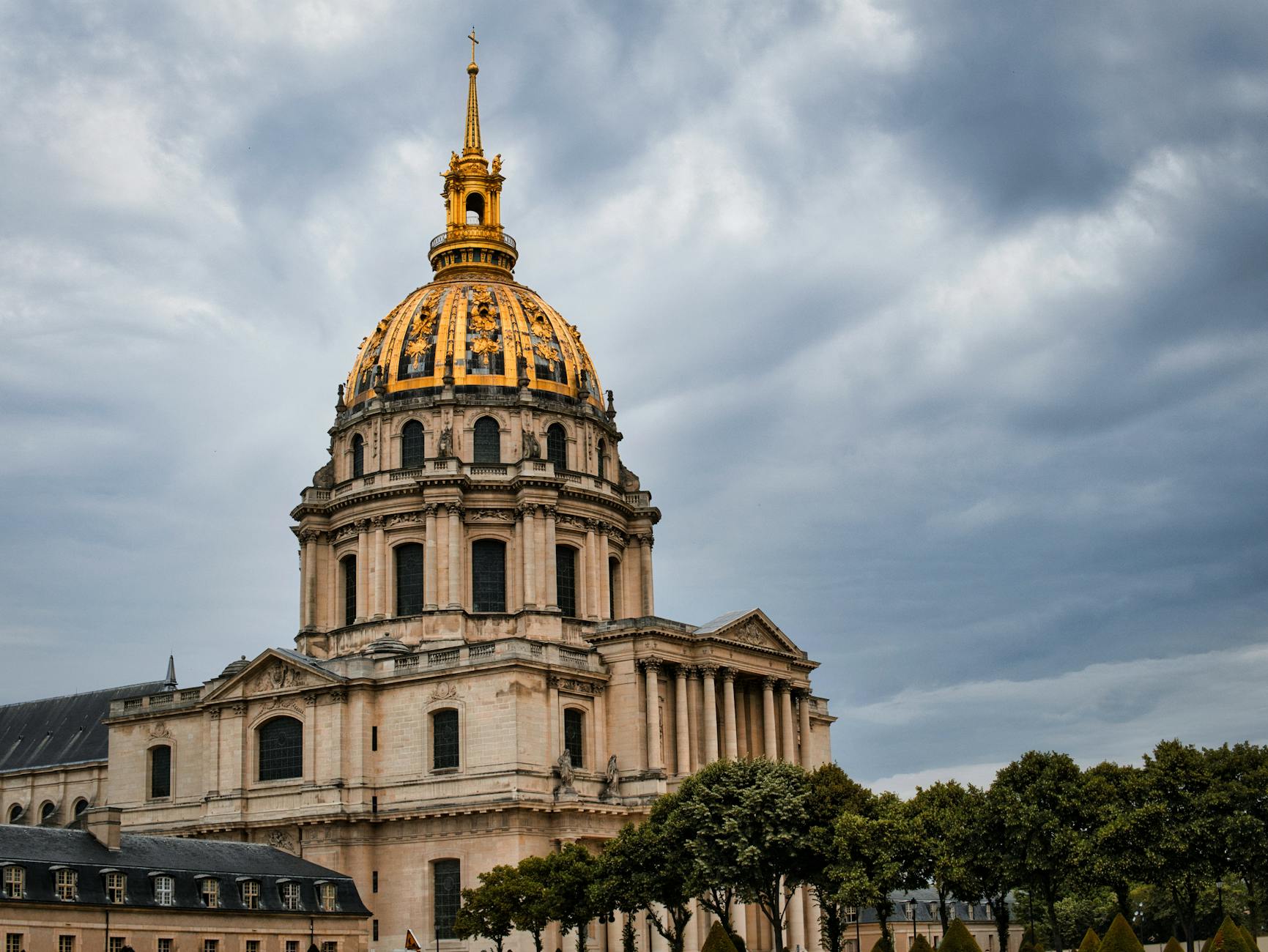Golden dome of Les Invalides viewed from street level against a dramatic cloudy sky