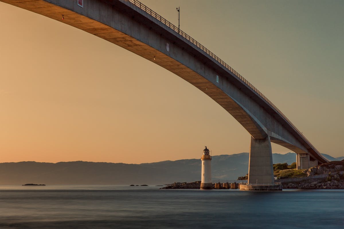 The Skye Bridge stretching over calm waters with a lighthouse at sunset