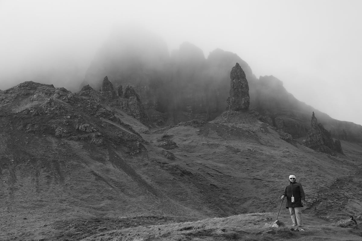 Hiker with trekking poles approaching the Old Man of Storr in misty conditions