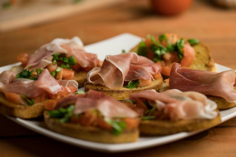 Italian bruschetta with prosciutto and fresh herbs on a wooden board