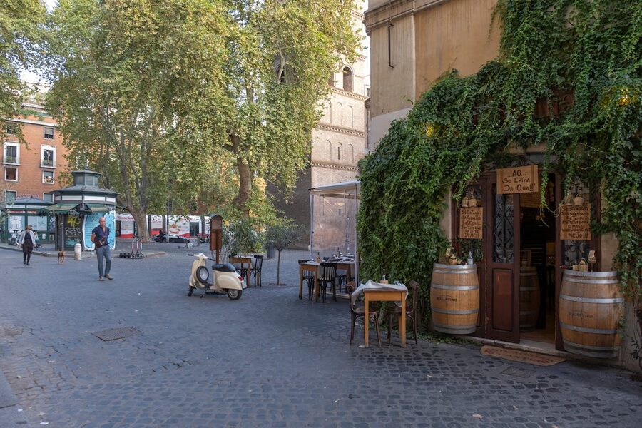 A charming street scene with an ivy-covered cafe, parked scooter, and people walking in Trastevere