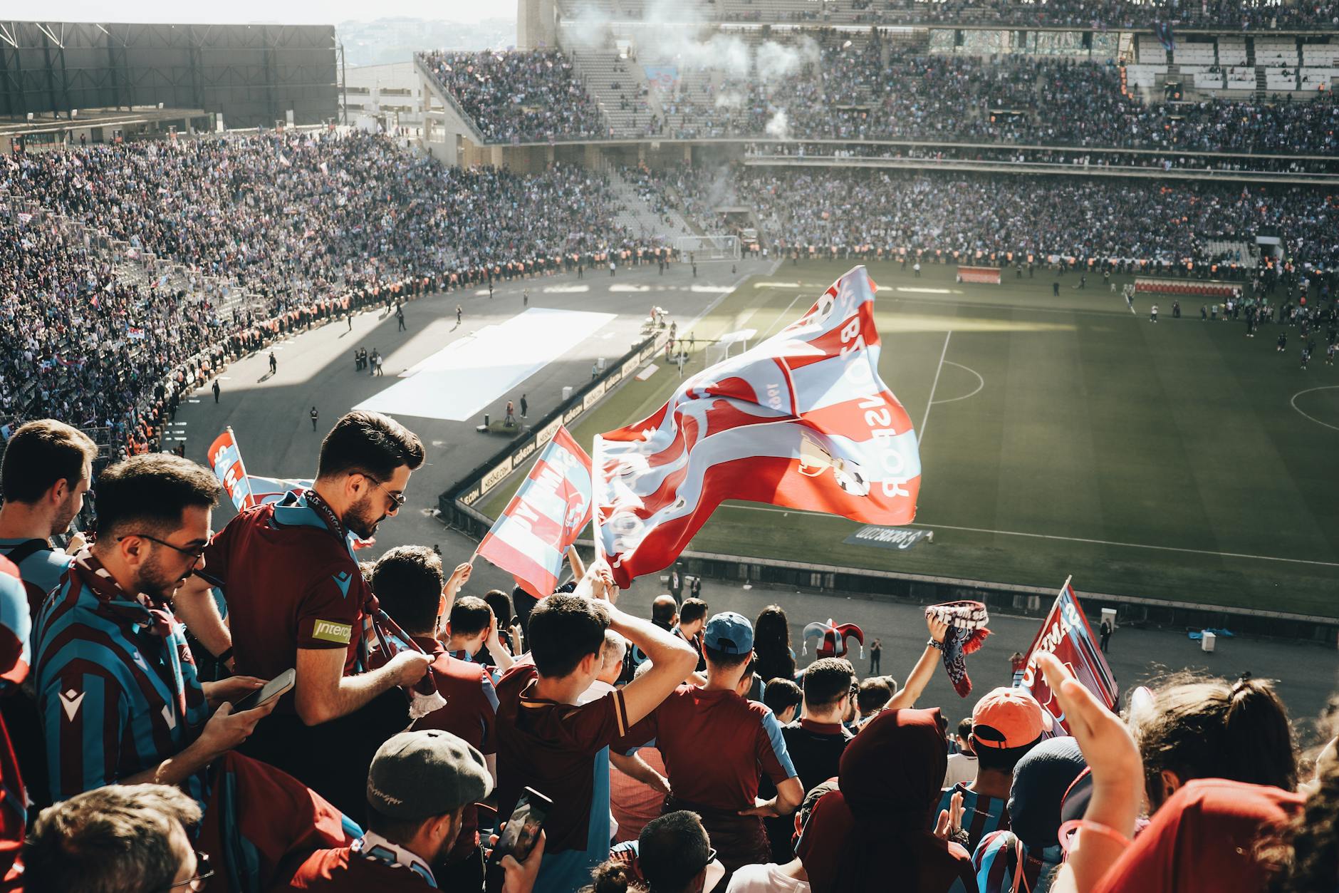 Vibrant crowd with flags cheering at a football stadium during the day