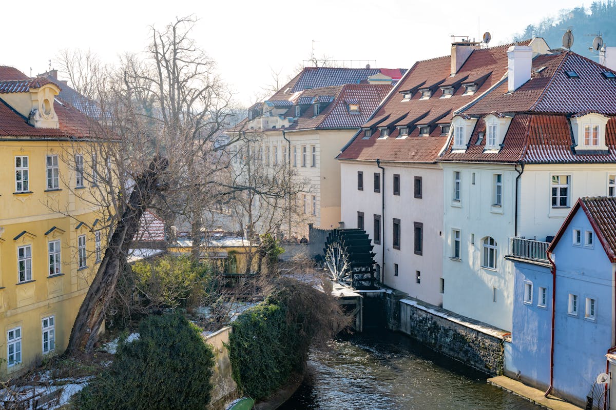 Serene view of historic Prague buildings along a canal with a watermill in winter