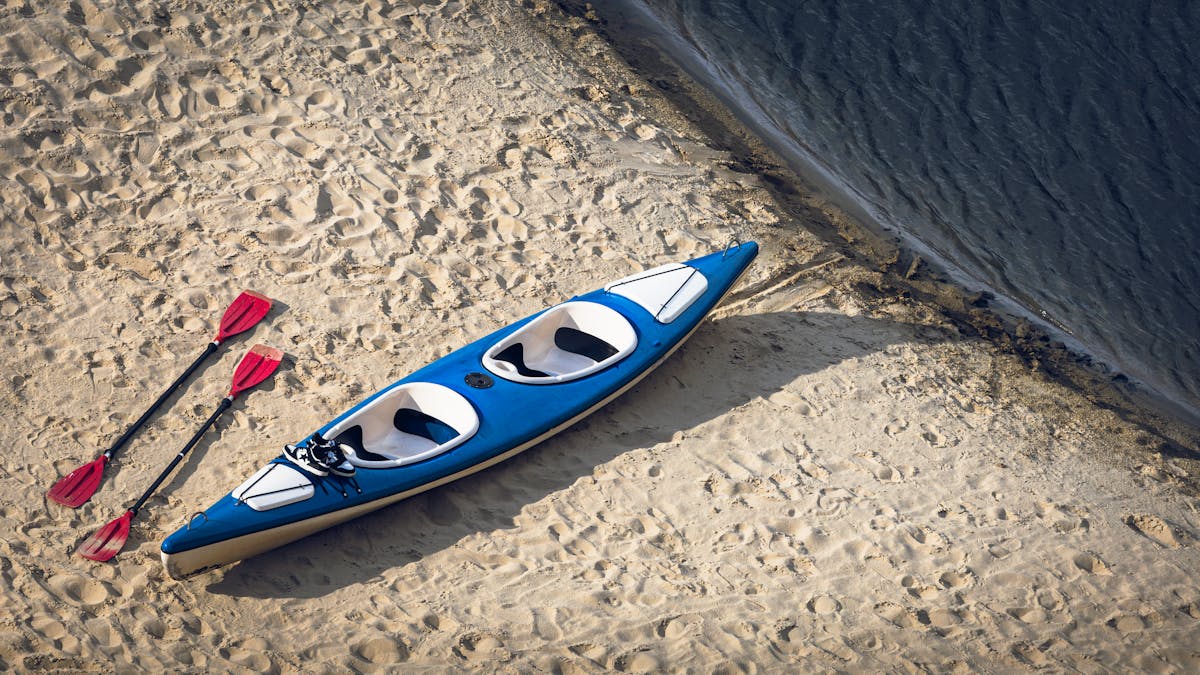 Blue kayak and red paddles resting on a sandy beach
