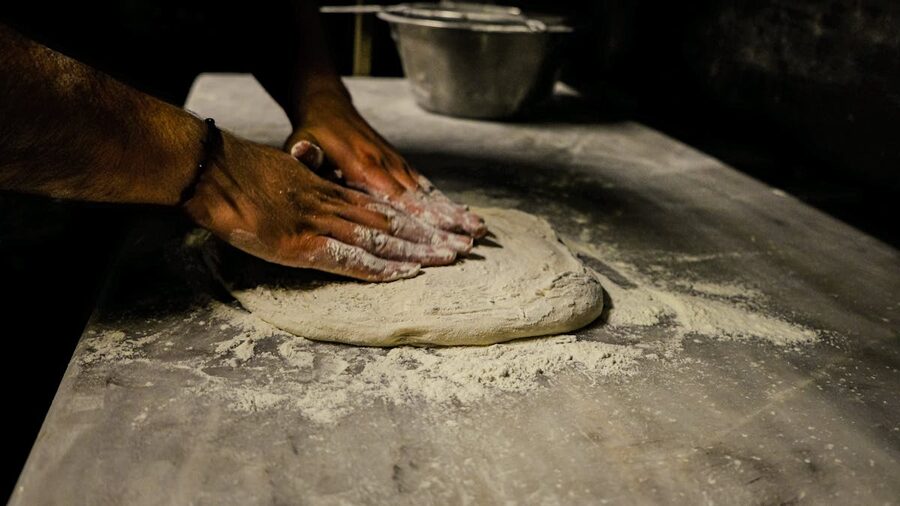 Close-up of a man kneading dough on a floured table in a traditional setting