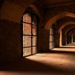 Dramatic lighting in an ancient stone corridor with gothic arches and barred gates