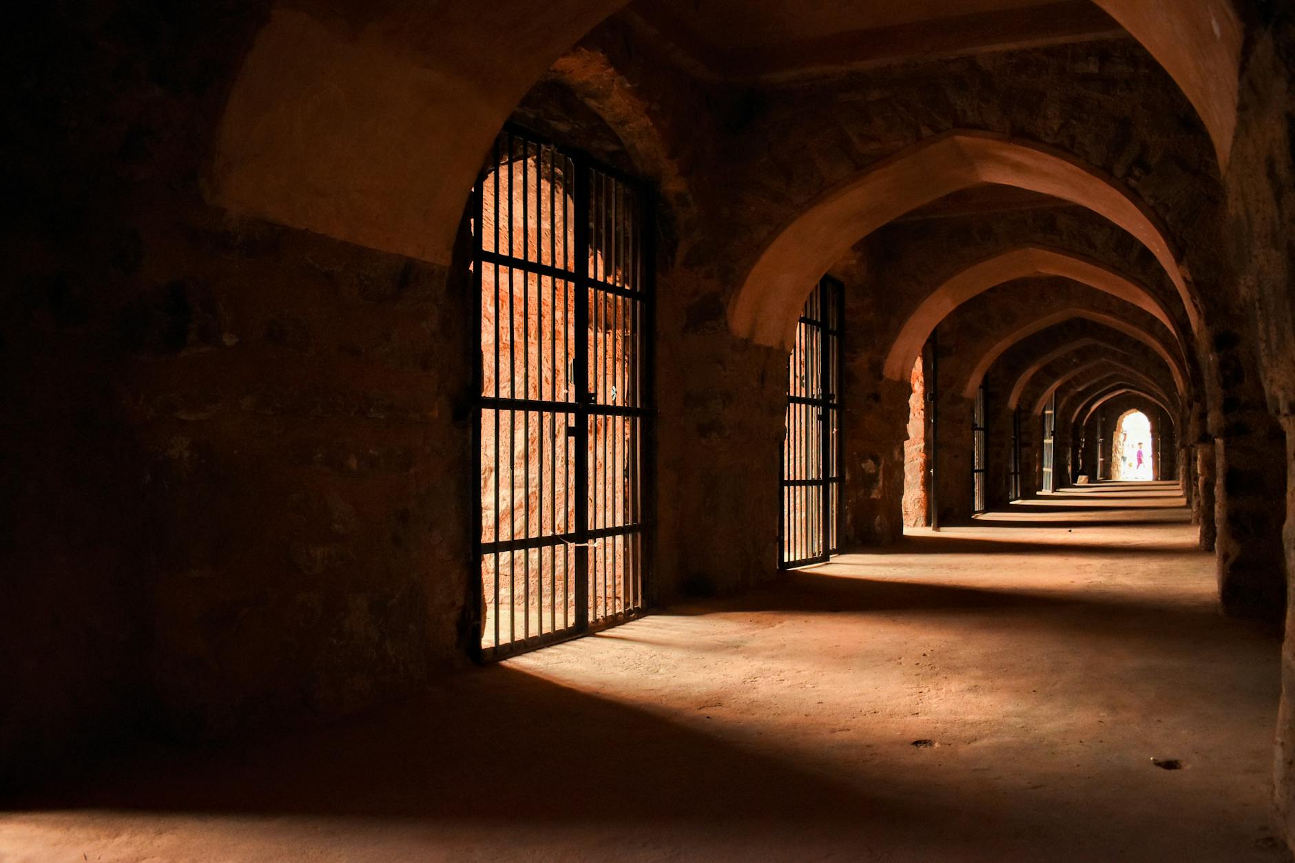 Dramatic lighting in an ancient stone corridor with gothic arches and barred gates