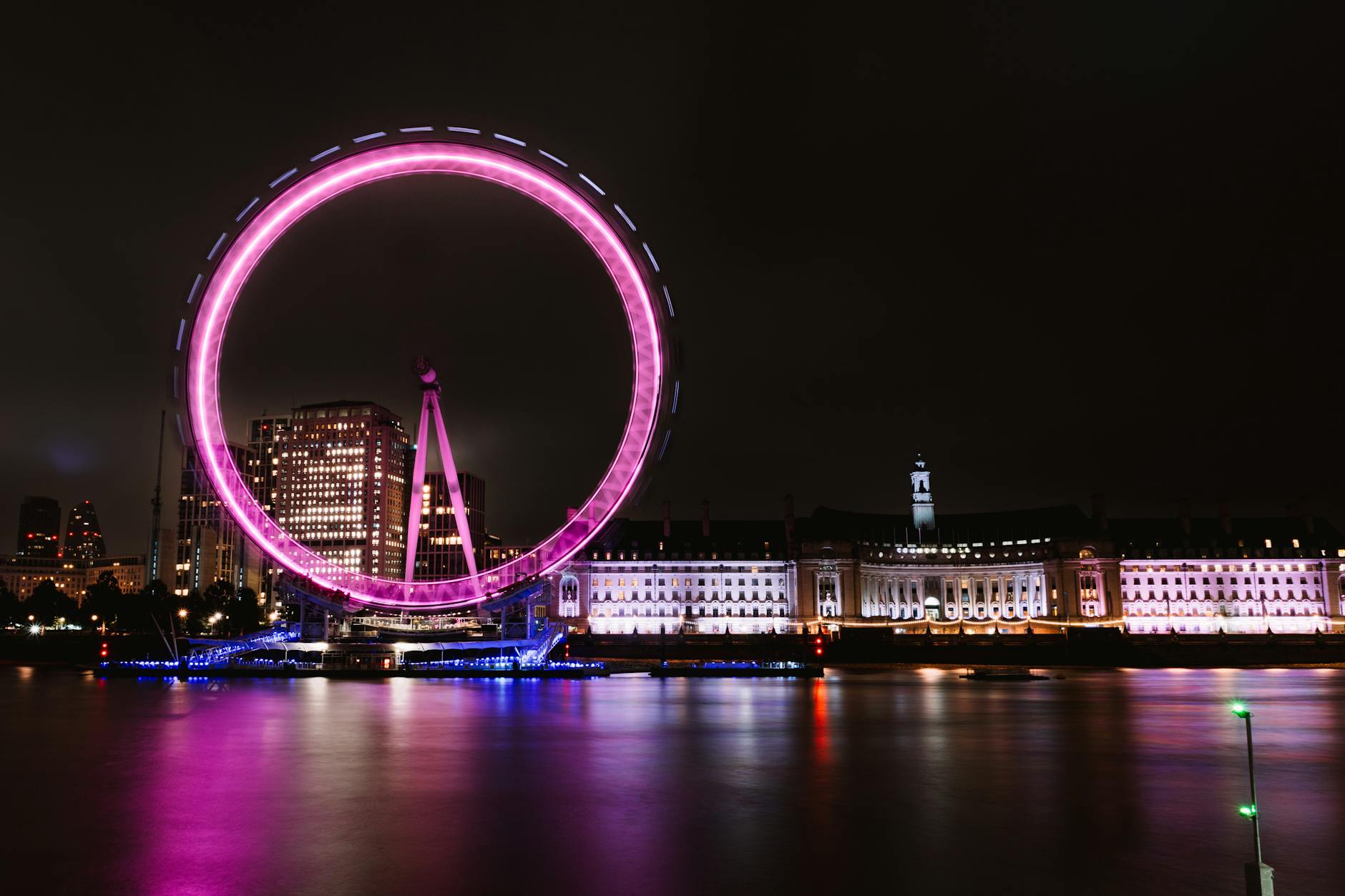 London Eye illuminated in pink along the Thames River at night