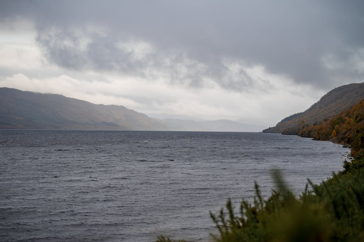 Panoramic view of Loch Ness in autumn with golden foliage and dramatic cloud formations over the dark water