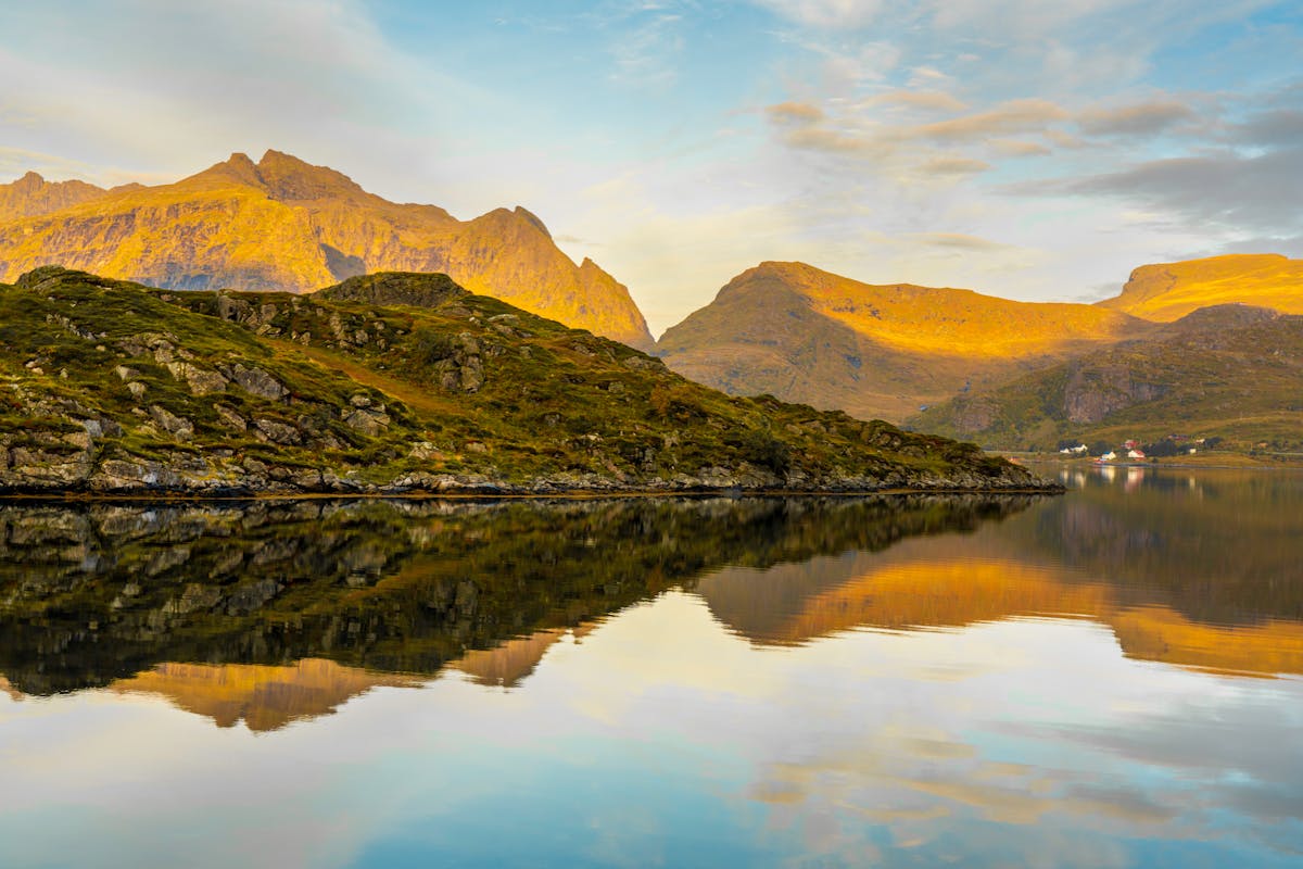 Lofoten mountains reflected in calm sea waters under golden sky