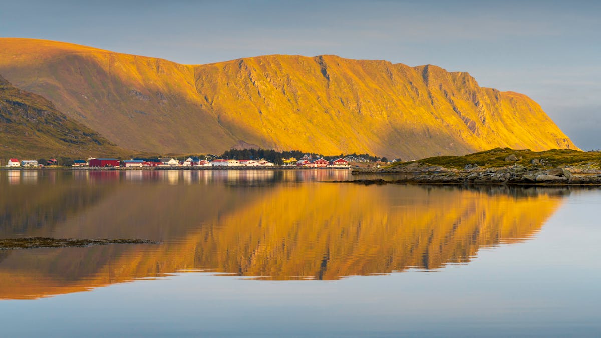 Coastal village reflecting in calm waters under golden mountains in Lofoten Norway