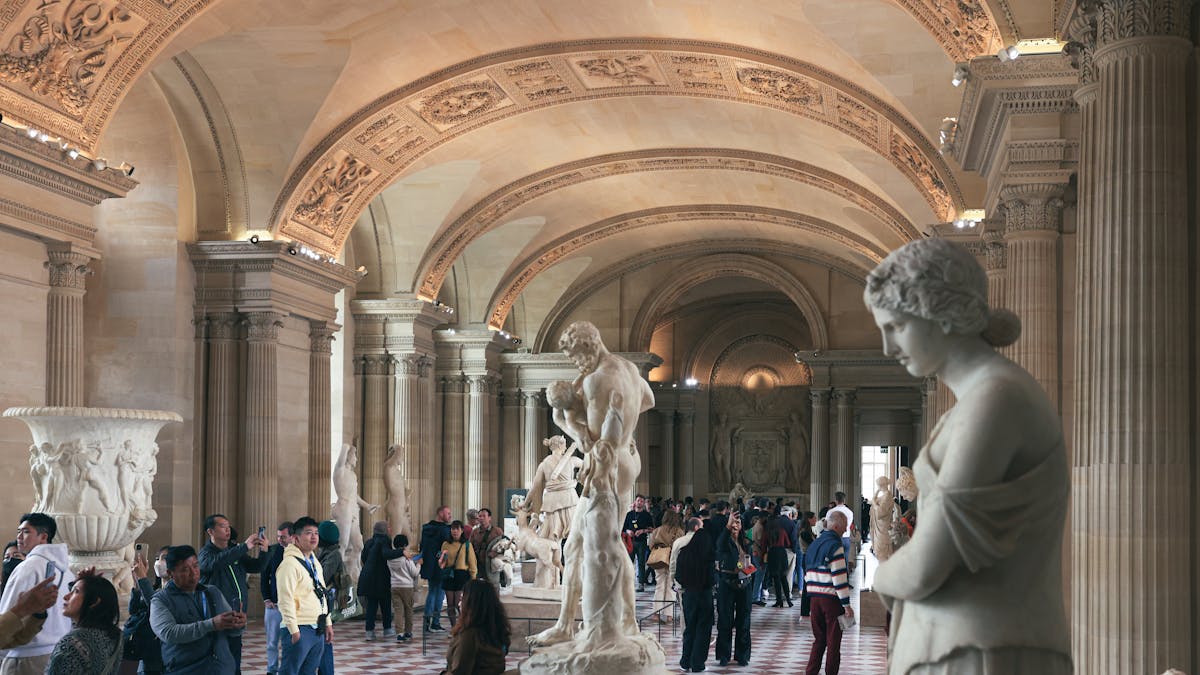 Visitors walking through a hall of classical sculptures at the Louvre