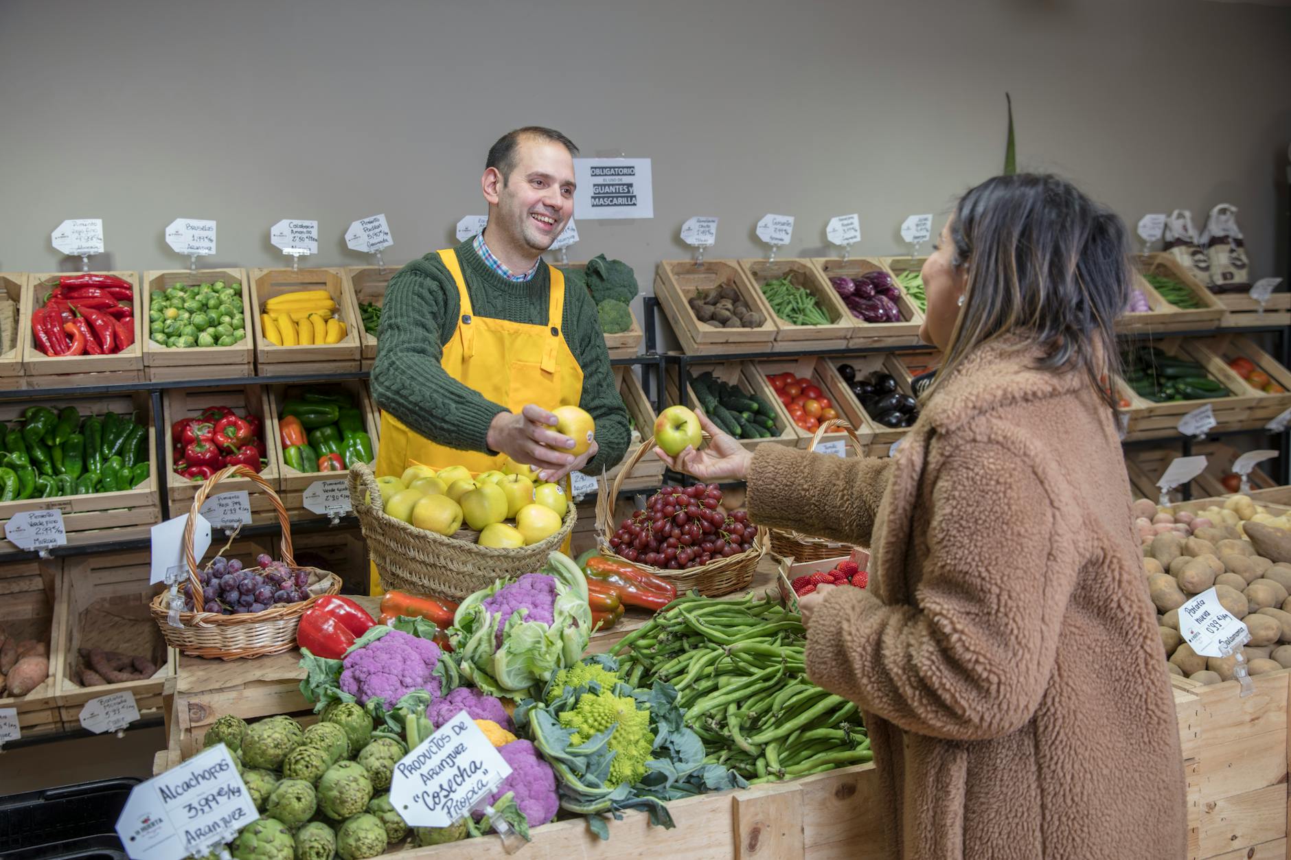 Man in yellow apron and woman exchanging fresh fruits at a market in Madrid