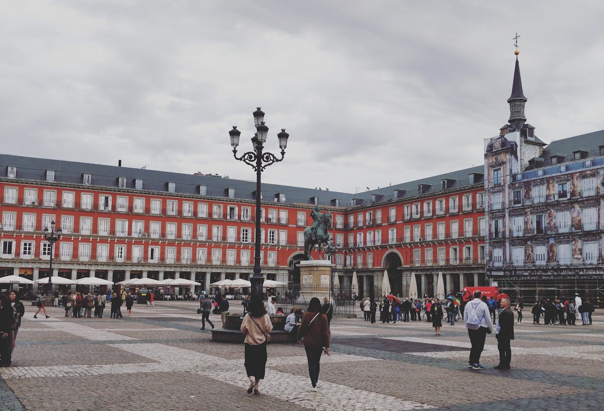 Plaza Mayor square in Madrid with ornate red facades and travelers walking across the cobblestones