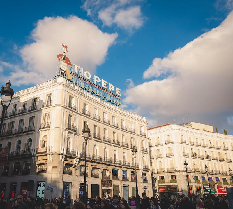 Crowded Puerta del Sol in Madrid with the iconic Tio Pepe sign under a bright sky