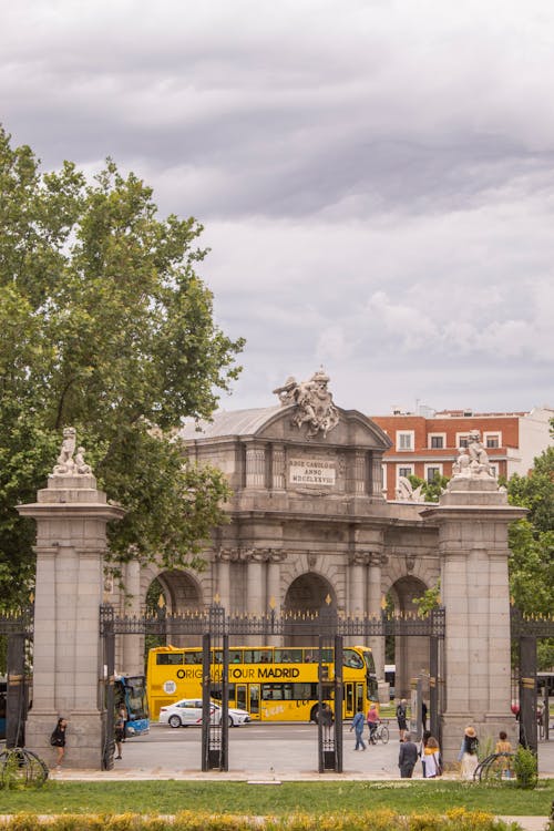 Yellow sightseeing tour bus passing through Puerta de Alcala in Madrid