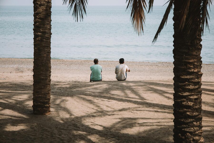 Two men sitting on Malaga beach under palm trees enjoying the sea view